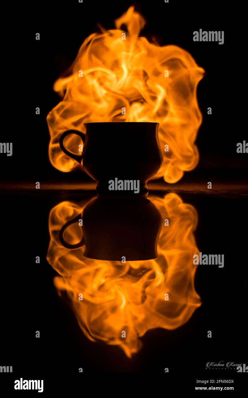 Mirrored silhouette of fire coming out of the cup isolated on the black ...