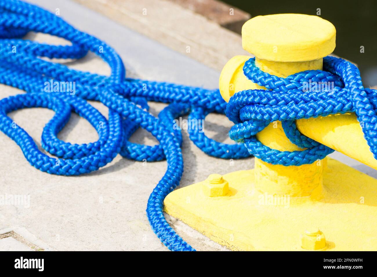 Blue rope and yellow mooring bollard, closeup and detail of seaport ...