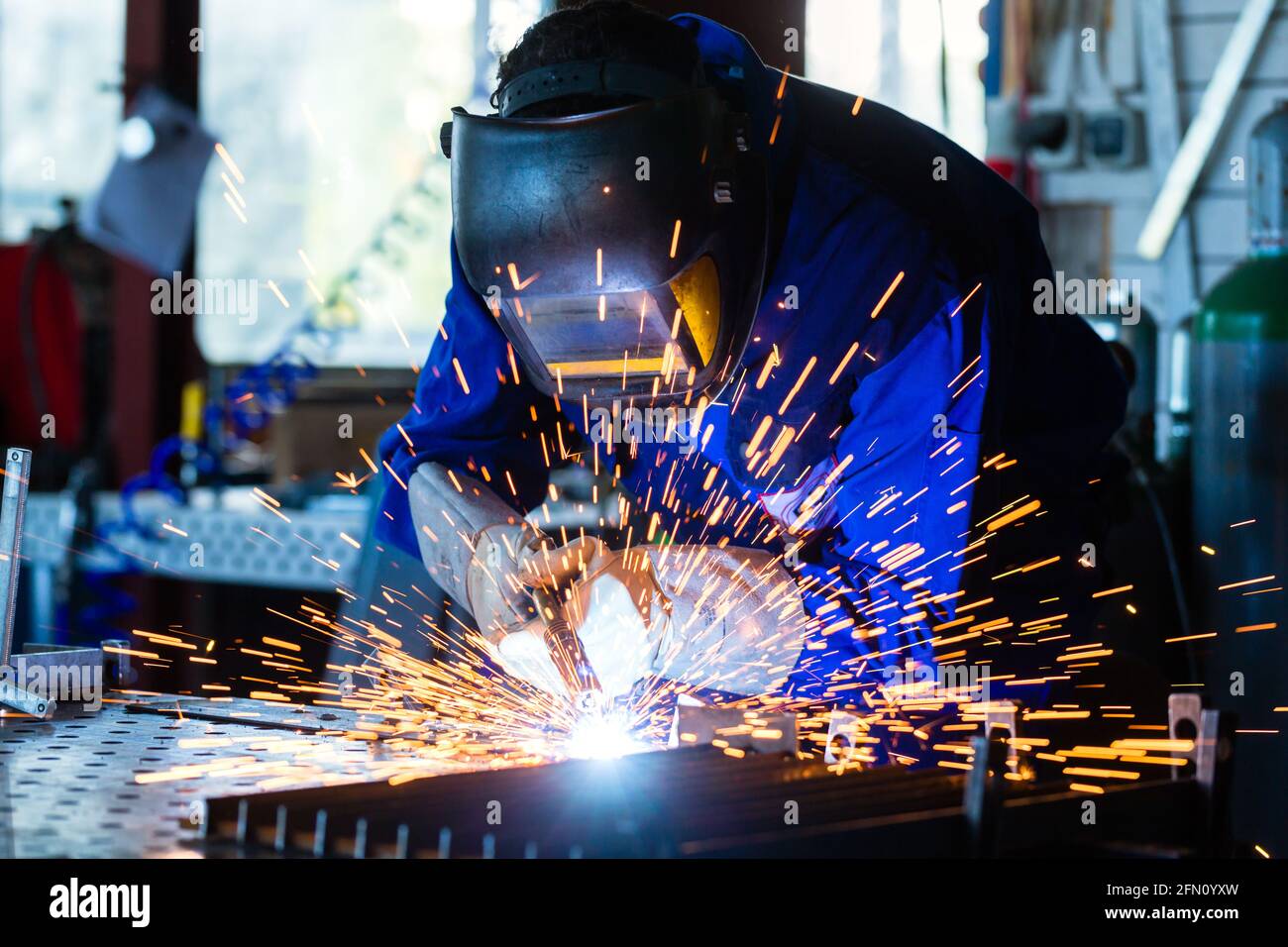 Welder bonding metal with welding device in workshop, lots of sparks to ...
