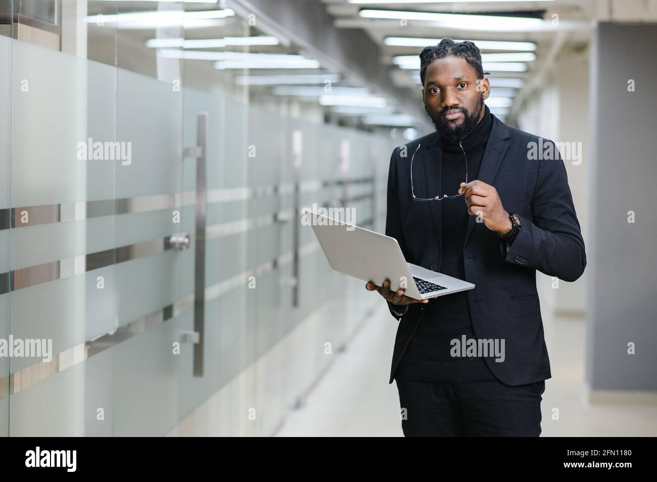 Smiling African American businessman standing alone in a large office ... Smiling African American businessman standing alone in a large office ...