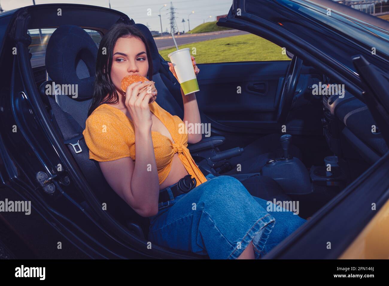 Model in blue jeans and orange top is eating hamburger and holding ...