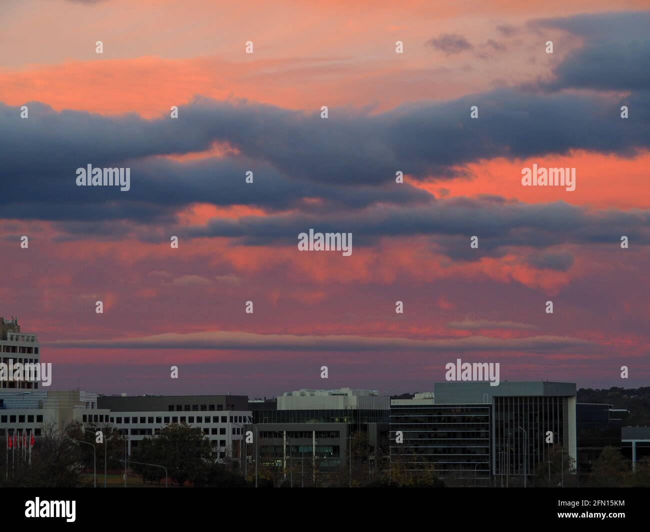 Sunset, rows of pink, blue grey and white clouds across glowing pink ...