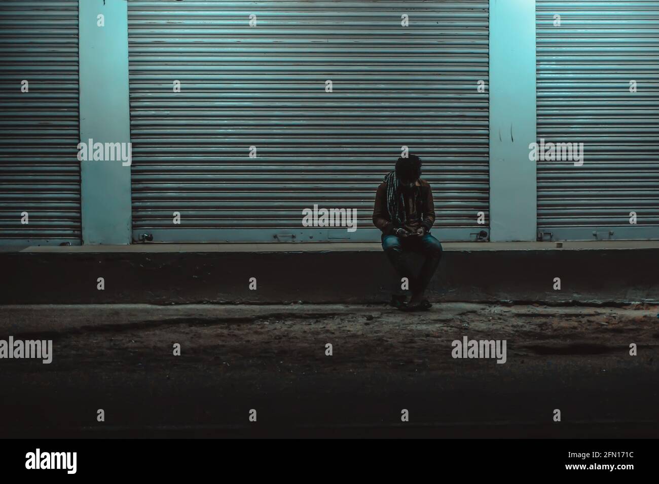 Lonely man sitting on the concrete surface against lighted wall ...