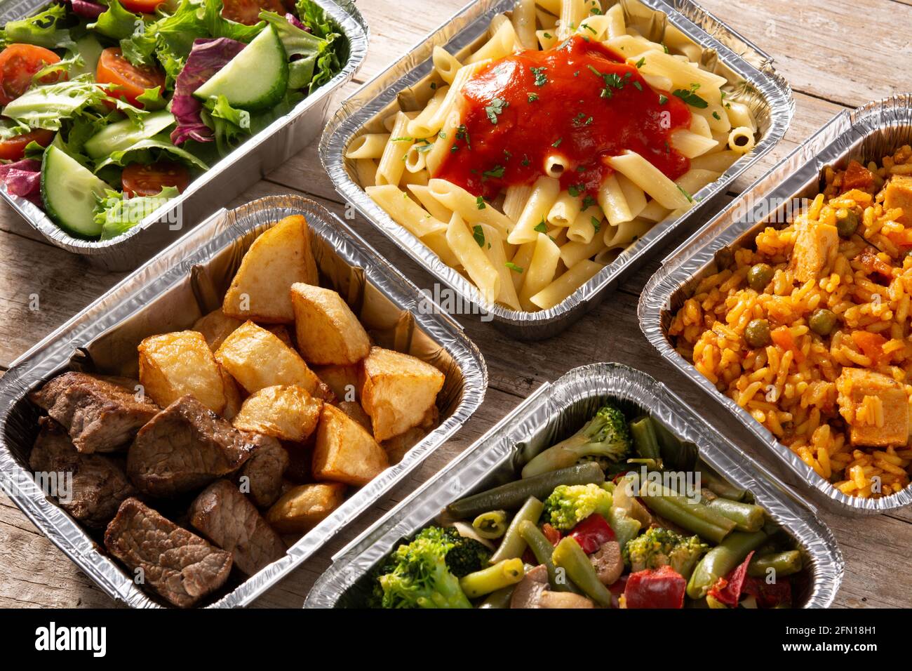 Take away healthy food in foil boxes on wooden table Stock Photo - Alamy