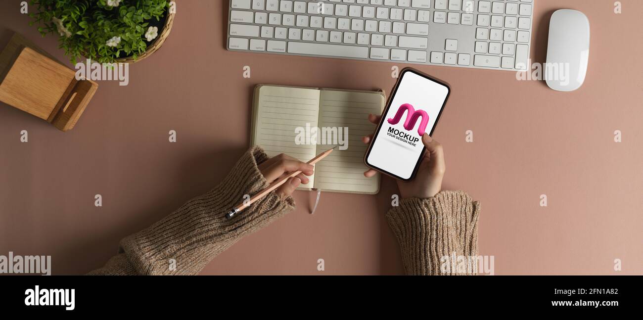 Overhead shot of female hand holding mock up smartphone while writing ...