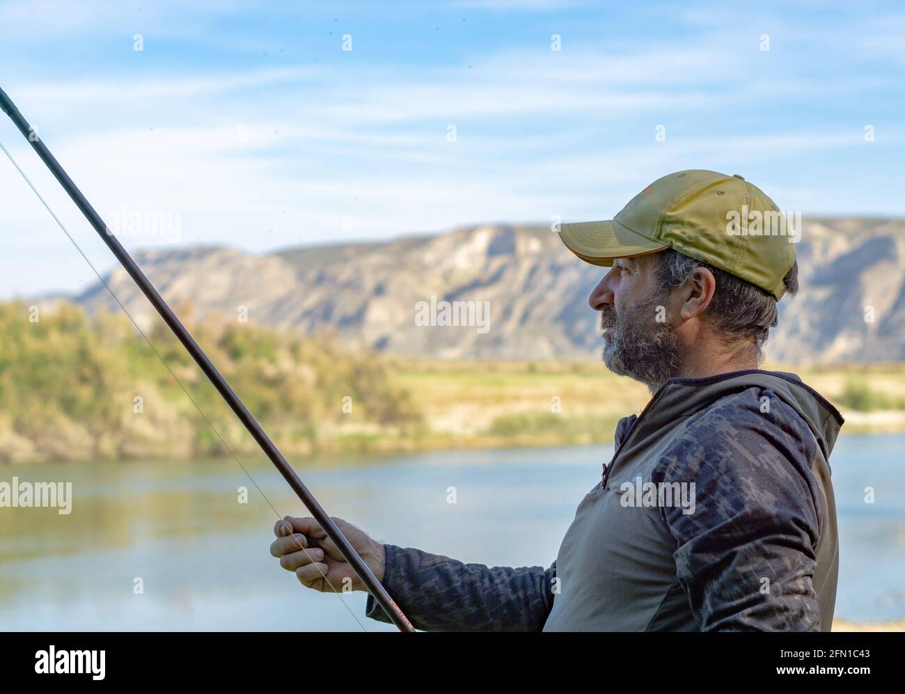Closeup shot of a Caucasian male with beard carp fishing in the river ...