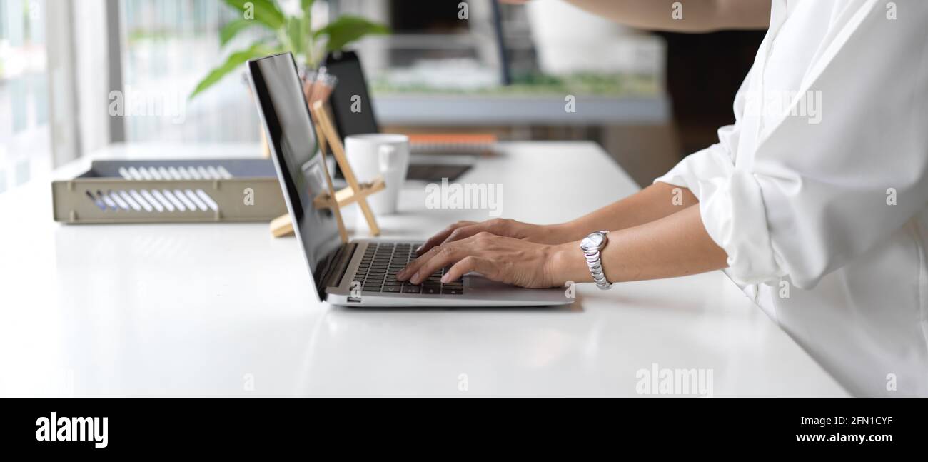 Side view of female hands typing on laptop keyboard on worktable with ...