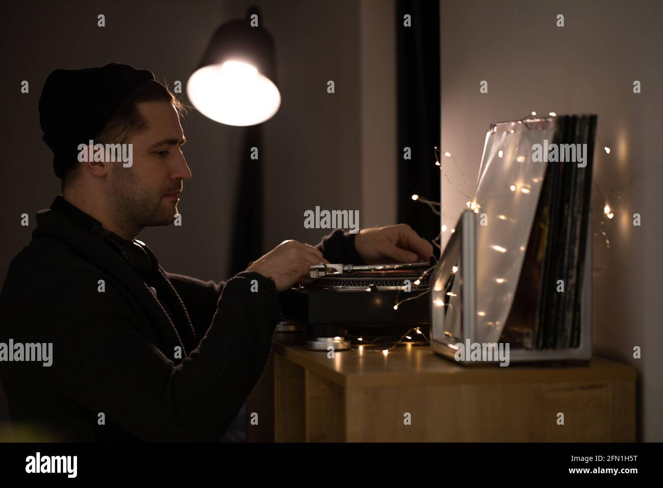 Young unshaven handsome hipster guy puts record on turntable backlit ...