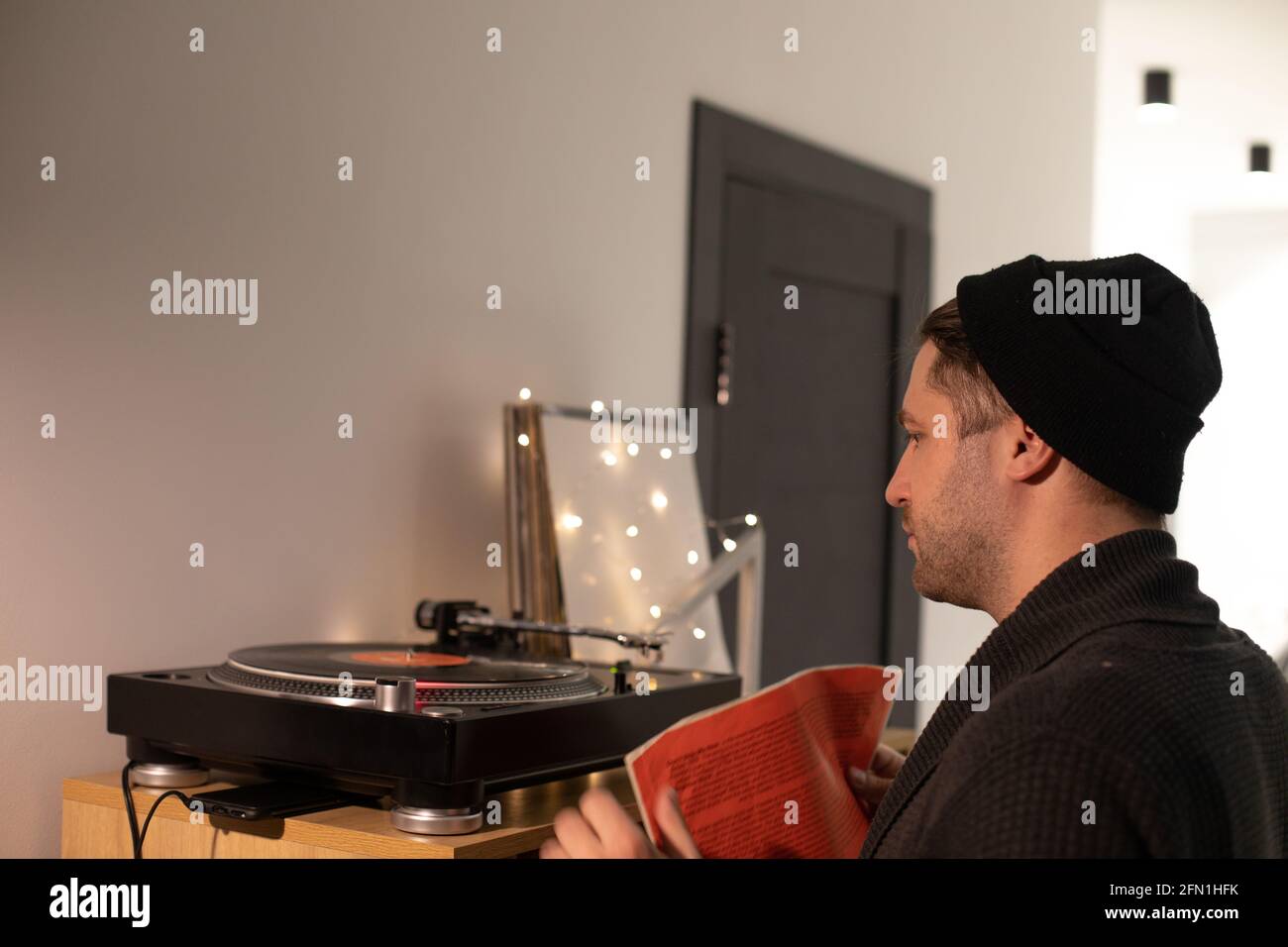 Young unshaven handsome hipster guy puts record on turntable from red ...