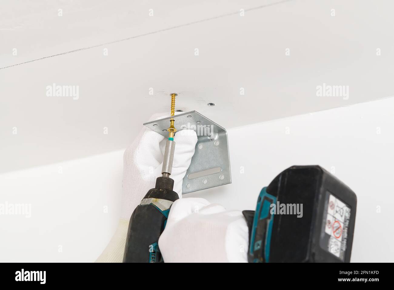 the master screws the metal corner to the concrete ceiling using a ...