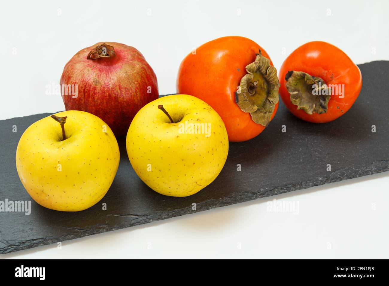 Yellow apples, a pomegranate and ripe persimmon fruits on the black ...