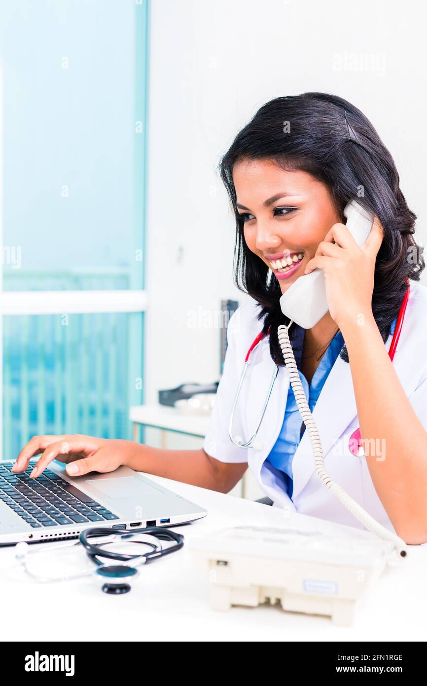 Asian female doctor working and telephoning in office or medical ...