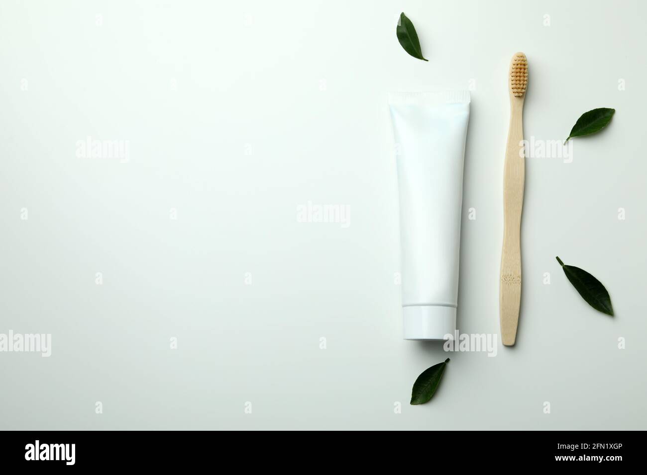 Eco friendly toothbrush, tube of toothpaste and leaves on white ...