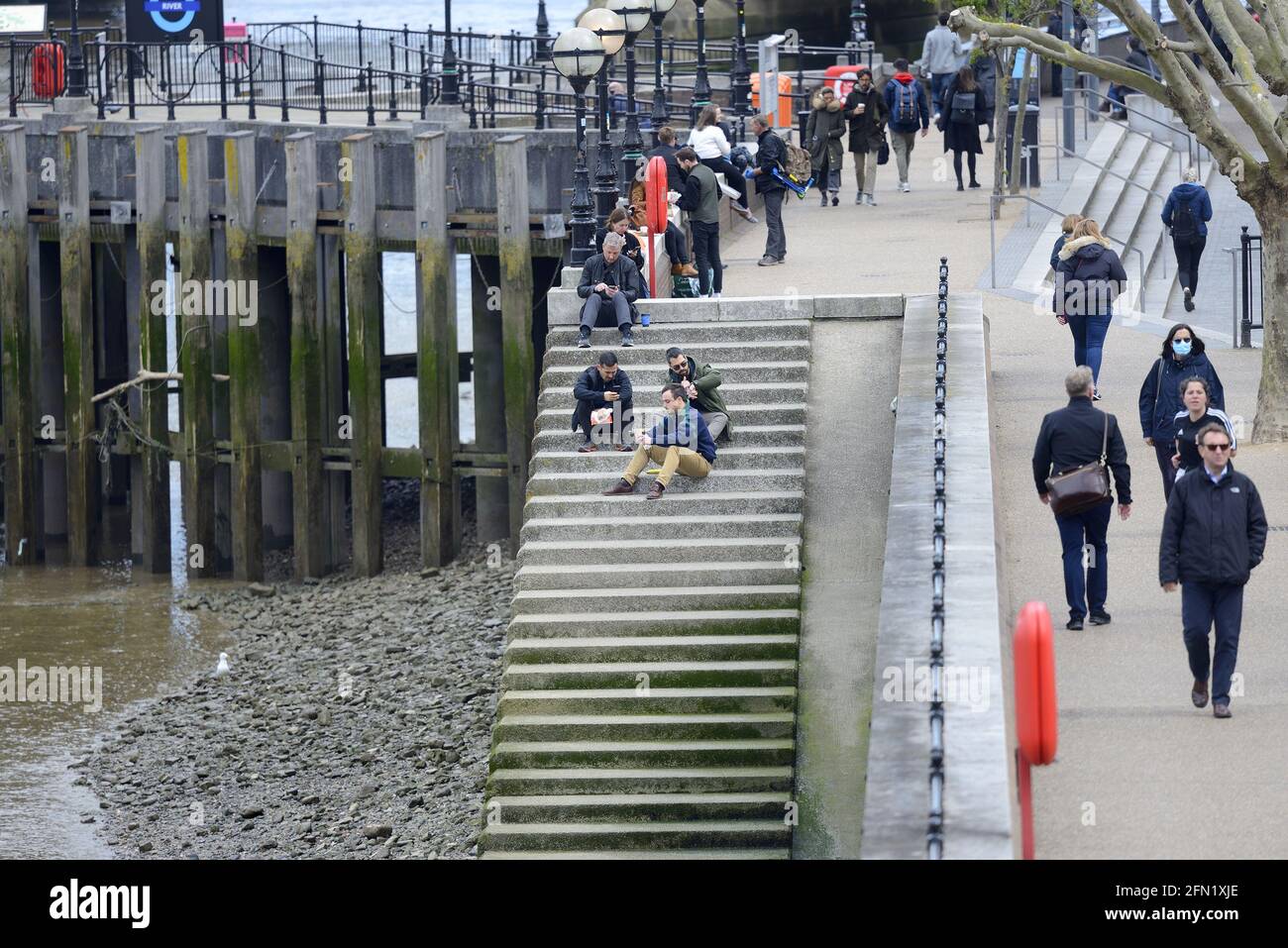London, England, UK. People walking along the South Bank and sitting on ...
