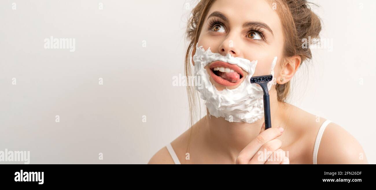 Beautiful young caucasian smiling woman shaving her face with razor sticking out tongue looking ...
