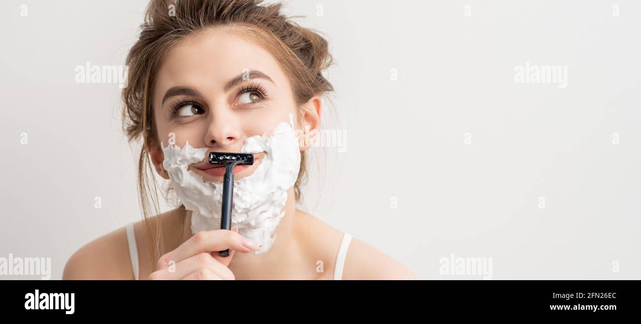 Beautiful young caucasian smiling woman shaving her face with razor looking up on white ...