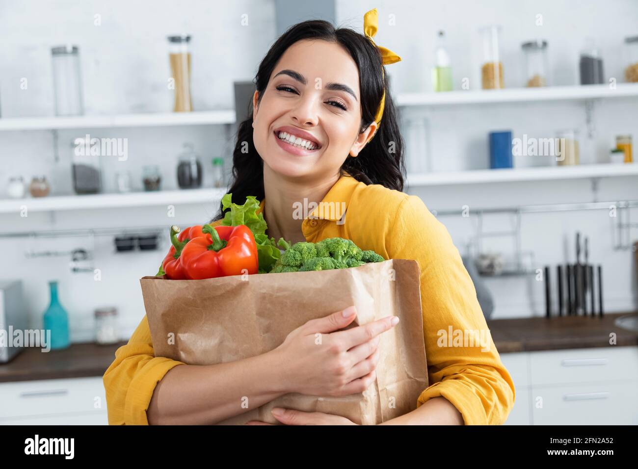 happy brunette woman hugging paper bag with fresh groceries Stock Photo ...