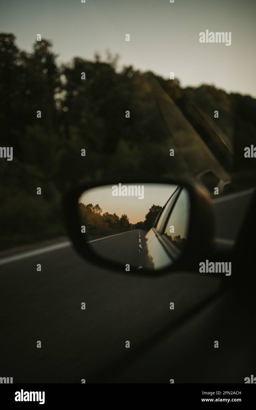 Vertical shot of a car side view mirror reflecting the asphalt road ...