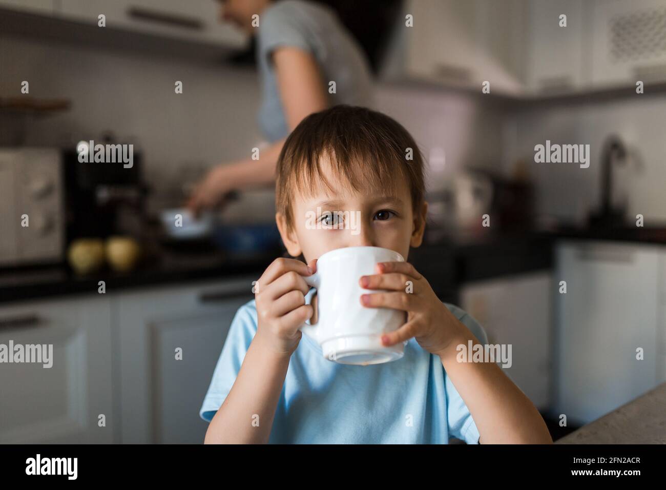 Child is drinking tea from mug and looking at camera Stock Photo - Alamy