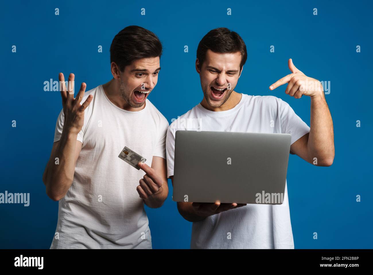 Excited two guys screaming while posing with laptop and credit card ...