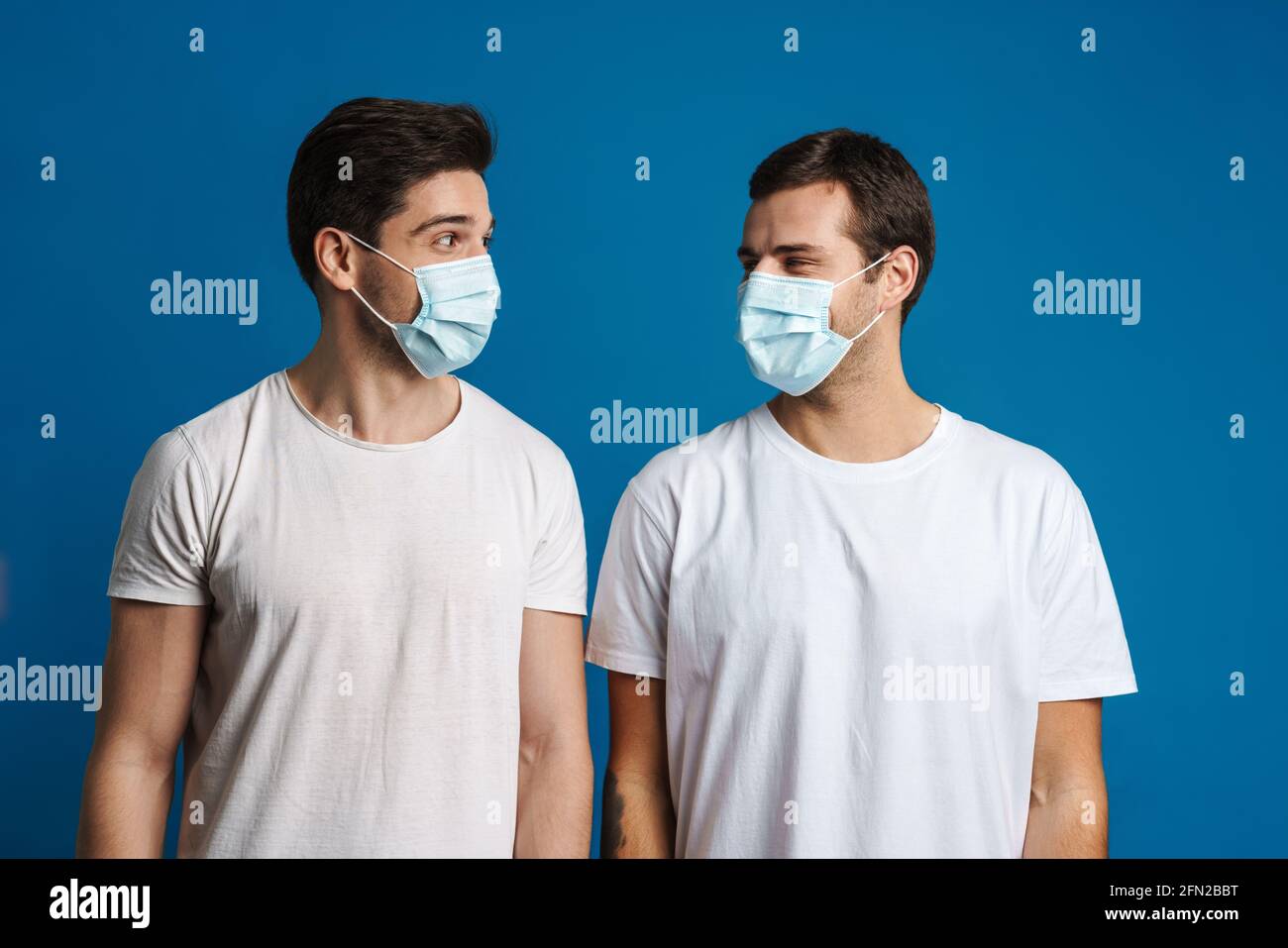 Pleased brunette two guys in face masks posing and looking at each ...