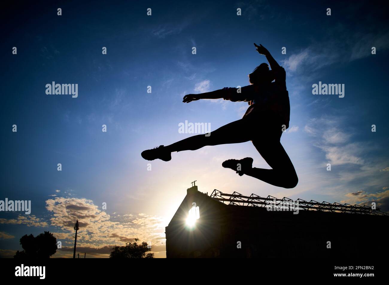 Silhouette of a person jumping and flexing in the air against a bright ...
