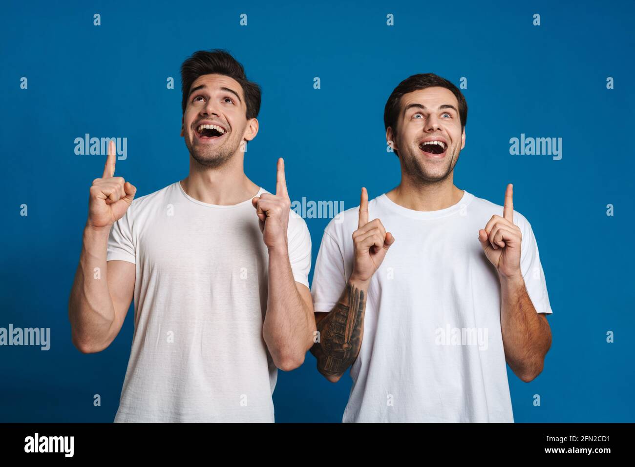 Excited unshaven two guys exclaiming while pointing fingers upward ...