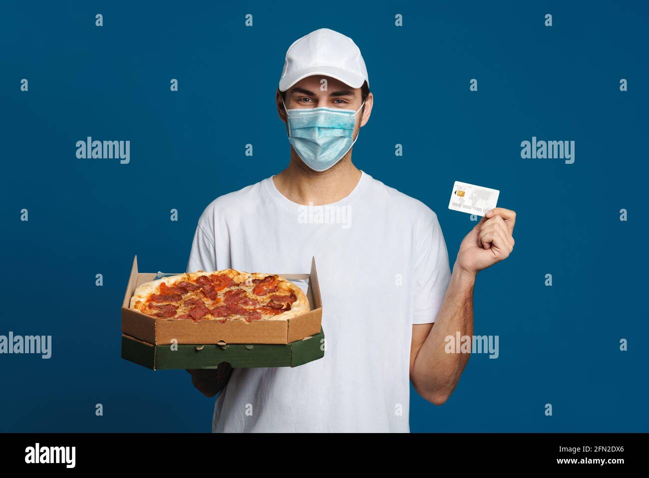 Happy delivery man in face mask posing with pizza and credit card ...
