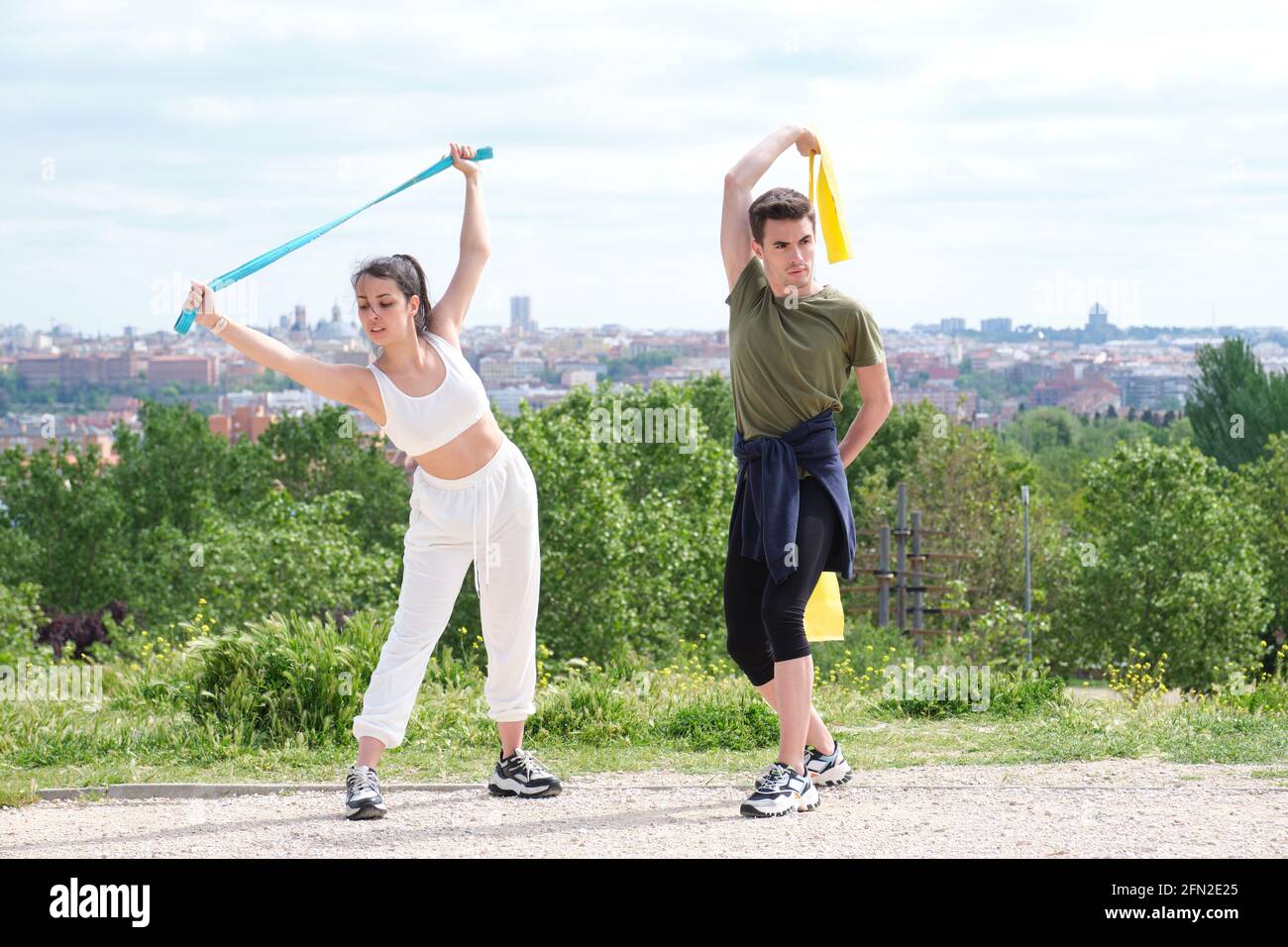 Young sporty couple exercising with rubber bands outdoors. Stretching exercises with elastic ...