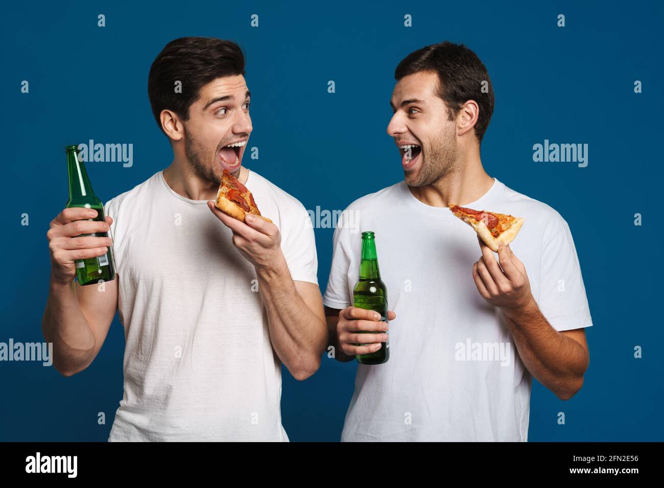Excited unshaven two guys eating pizza while drinking bear isolated ...
