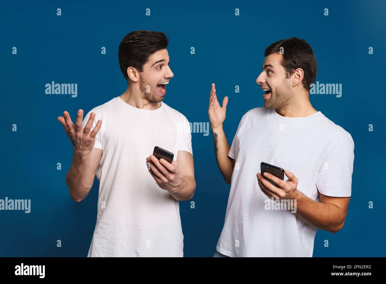 Delighted two guys expressing surprise while posing with smartphones ...