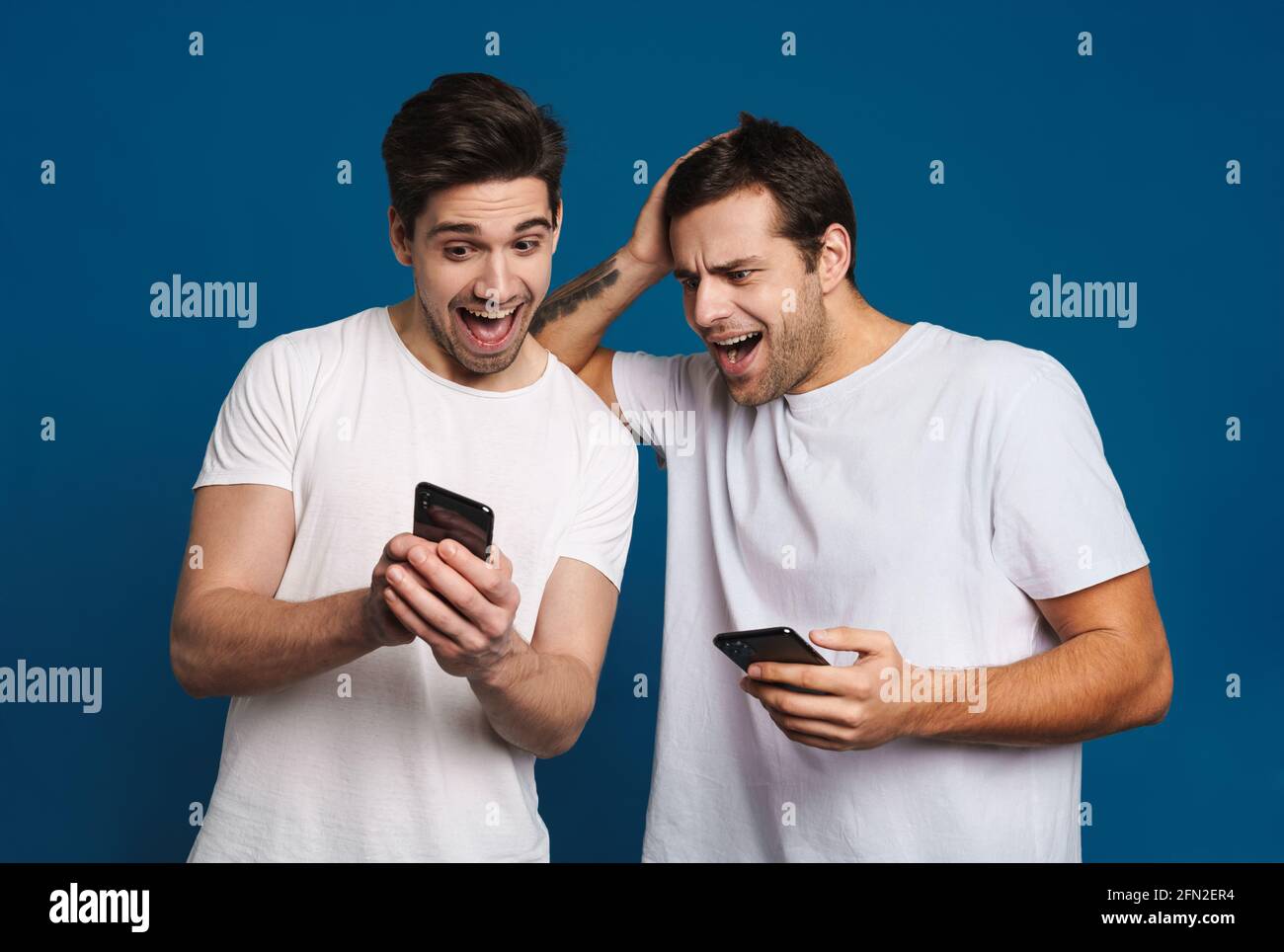 Delighted two guys expressing surprise while posing with smartphones ...