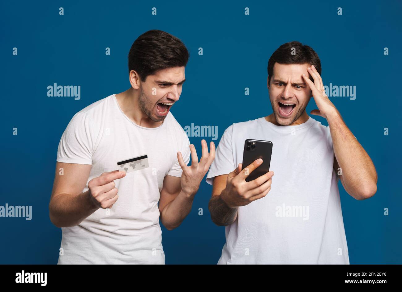 Furious two guys screaming while posing with credit card and mobile ...