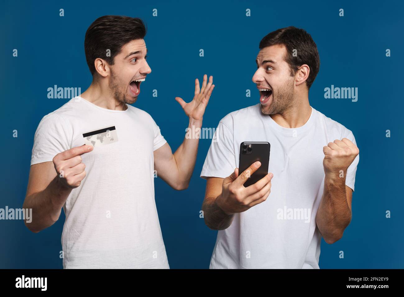 Delighted two guys screaming while posing with credit card and mobile ...