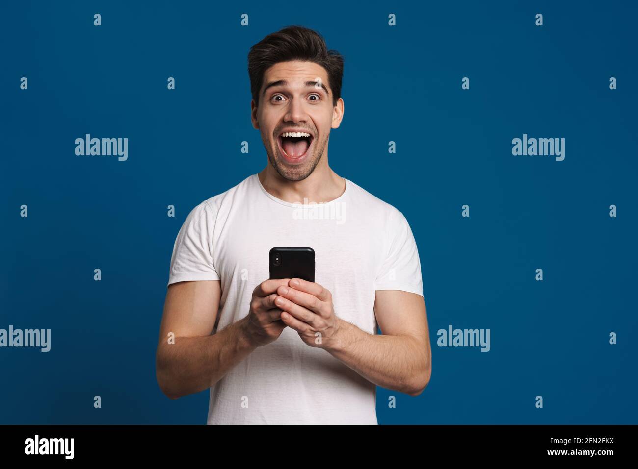 Delighted guy expressing surprise while using mobile phone isolated ...