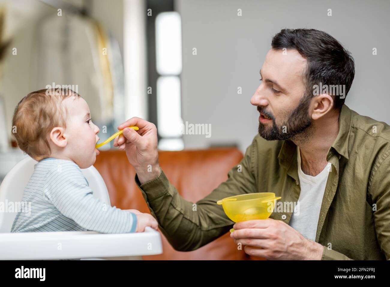 Father feeding his one year baby boy with a spoon. Dad feeding baby in ...