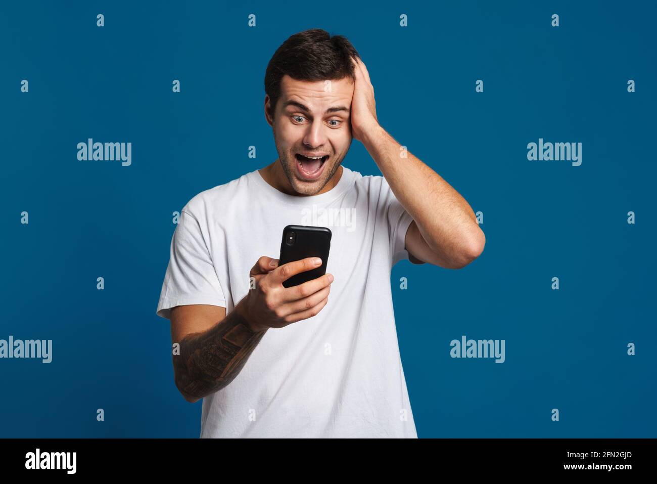 Delighted guy expressing surprise while using mobile phone isolated ...