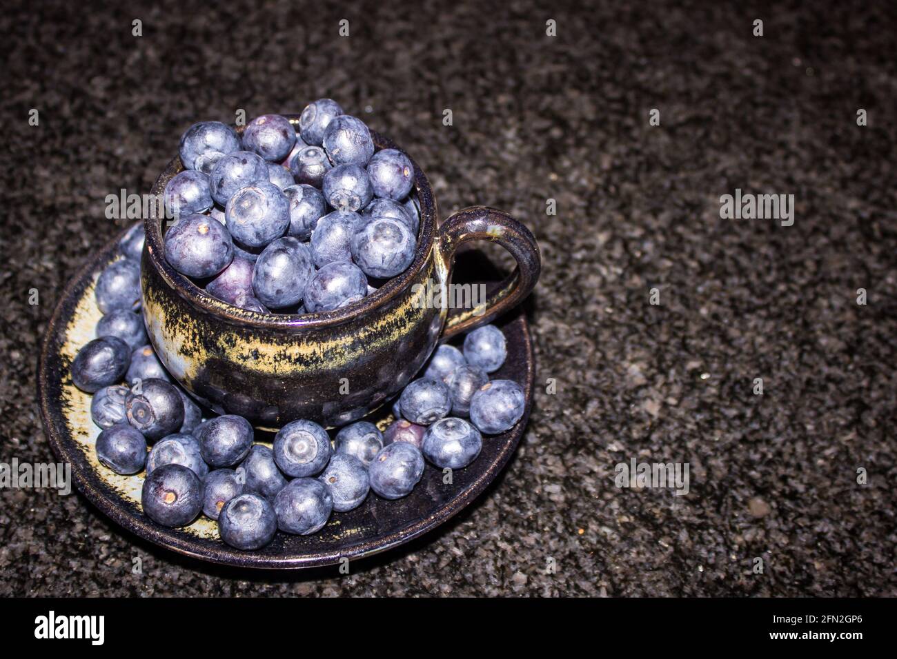 A black ceramic cup, filled to over spilling with large indigo-colored ...