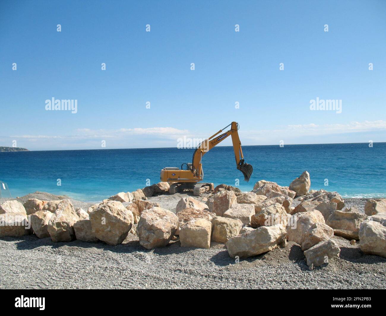Yellow backhoe with hydraulic piston arm against Mediterranean sea ...