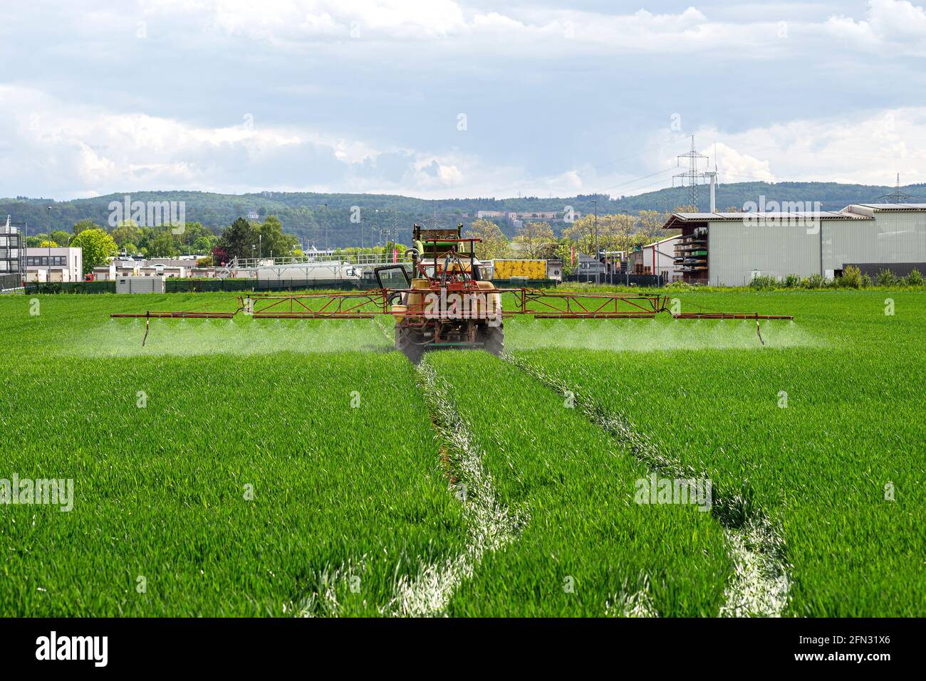 Spraying a crop field with a tractor that has a tank with spray nozzles ...