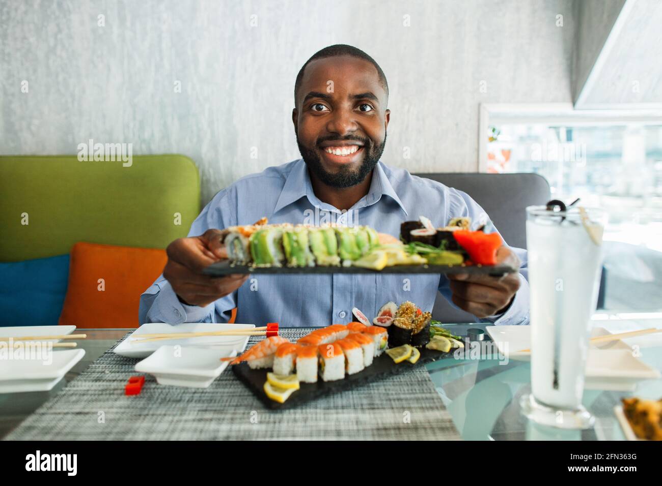 Young african business man sitting at sushi bar, demonstrating to the ...