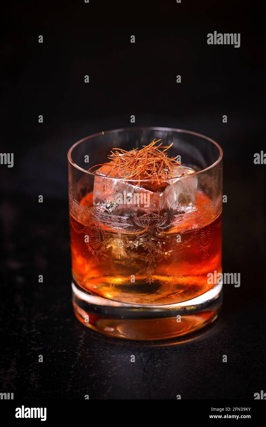 Negroni with big ice cube and saffron on top in vintage glass with dark ...