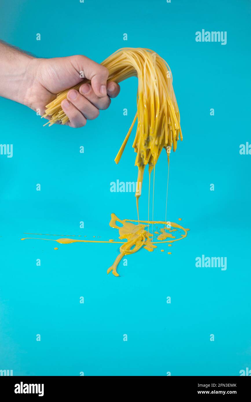 Hand holding half cooked spaghetti with dripping yellow paint ...