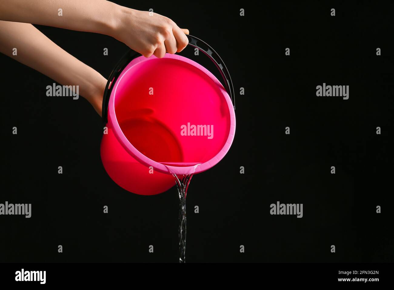 Woman pouring water from bucket on dark background Stock Photo - Alamy