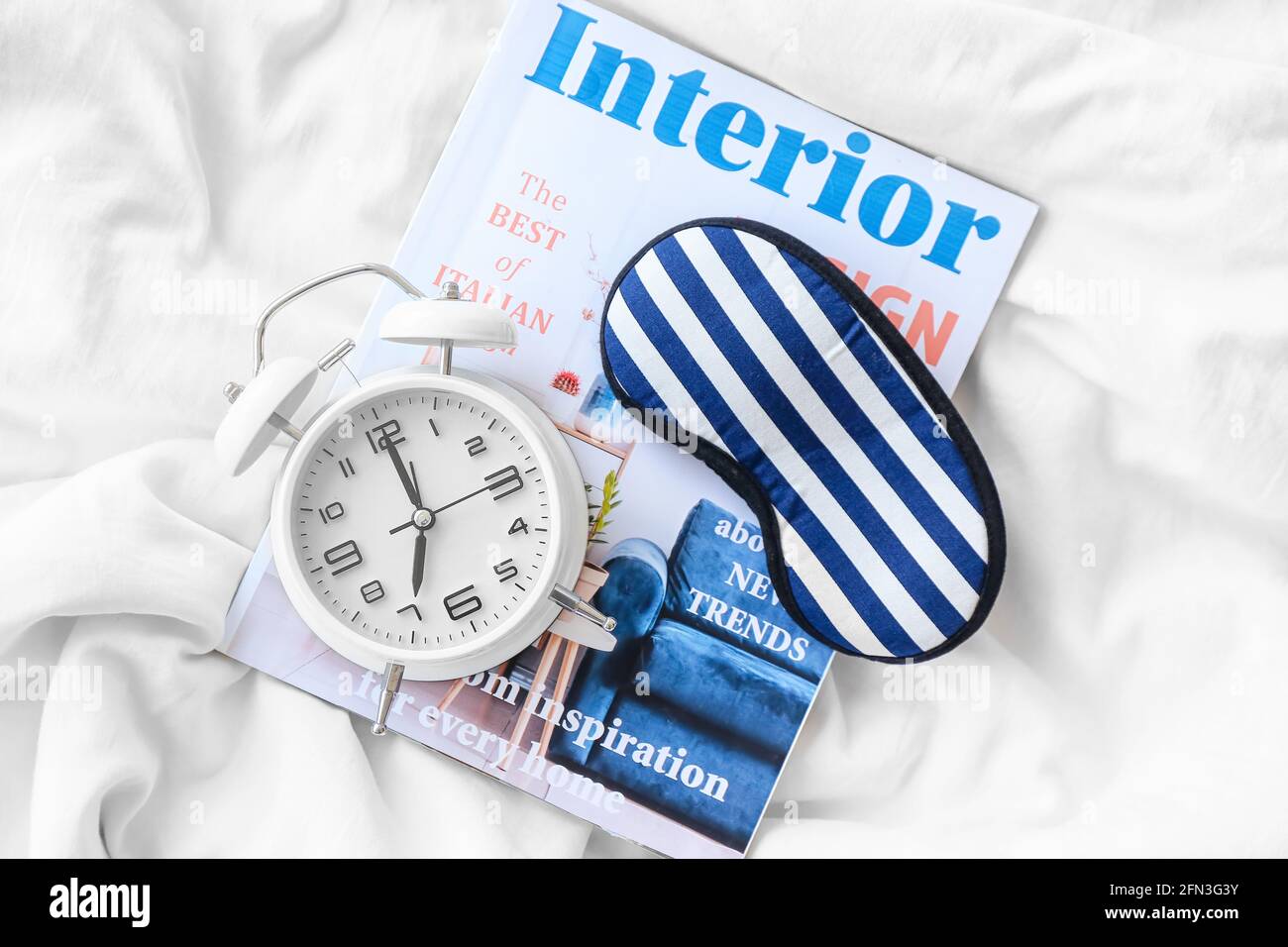 Alarm clock with sleeping mask and magazine on bed Stock Photo - Alamy