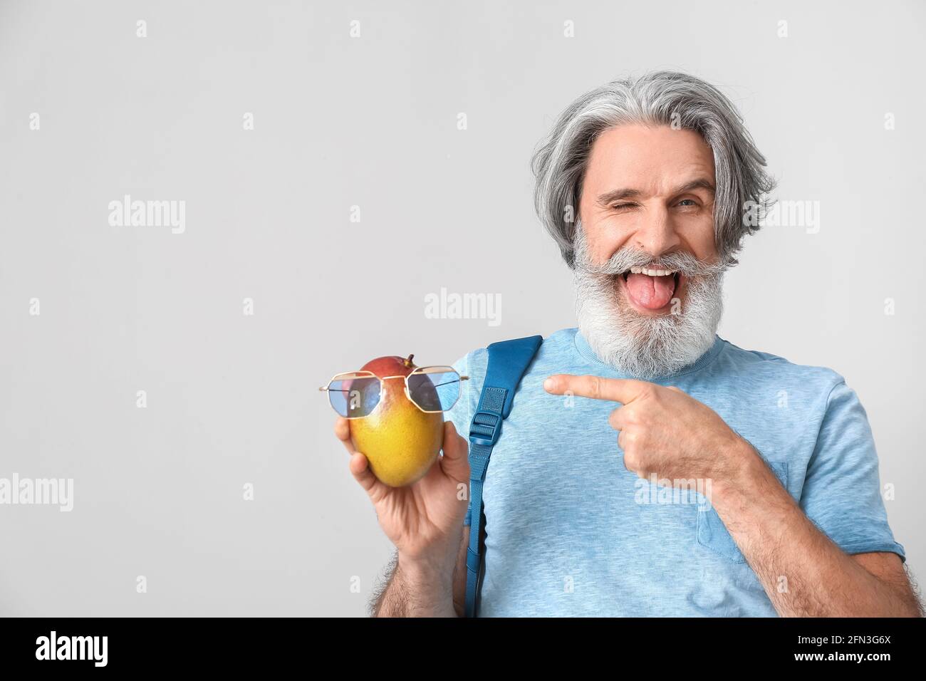 Senior man pointing at fresh mango on light background Stock Photo - Alamy