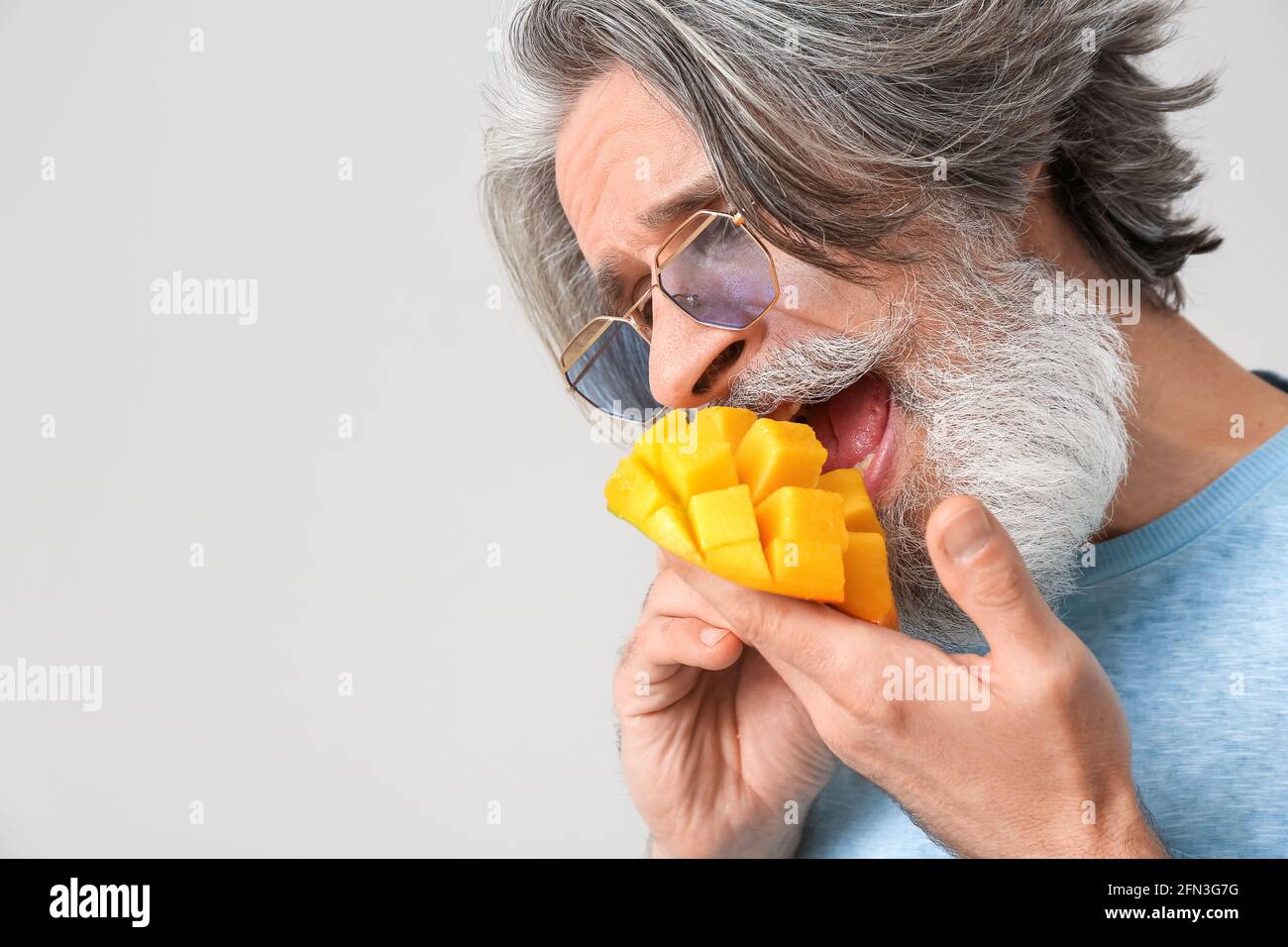 Senior man eating cut mango on light background Stock Photo - Alamy