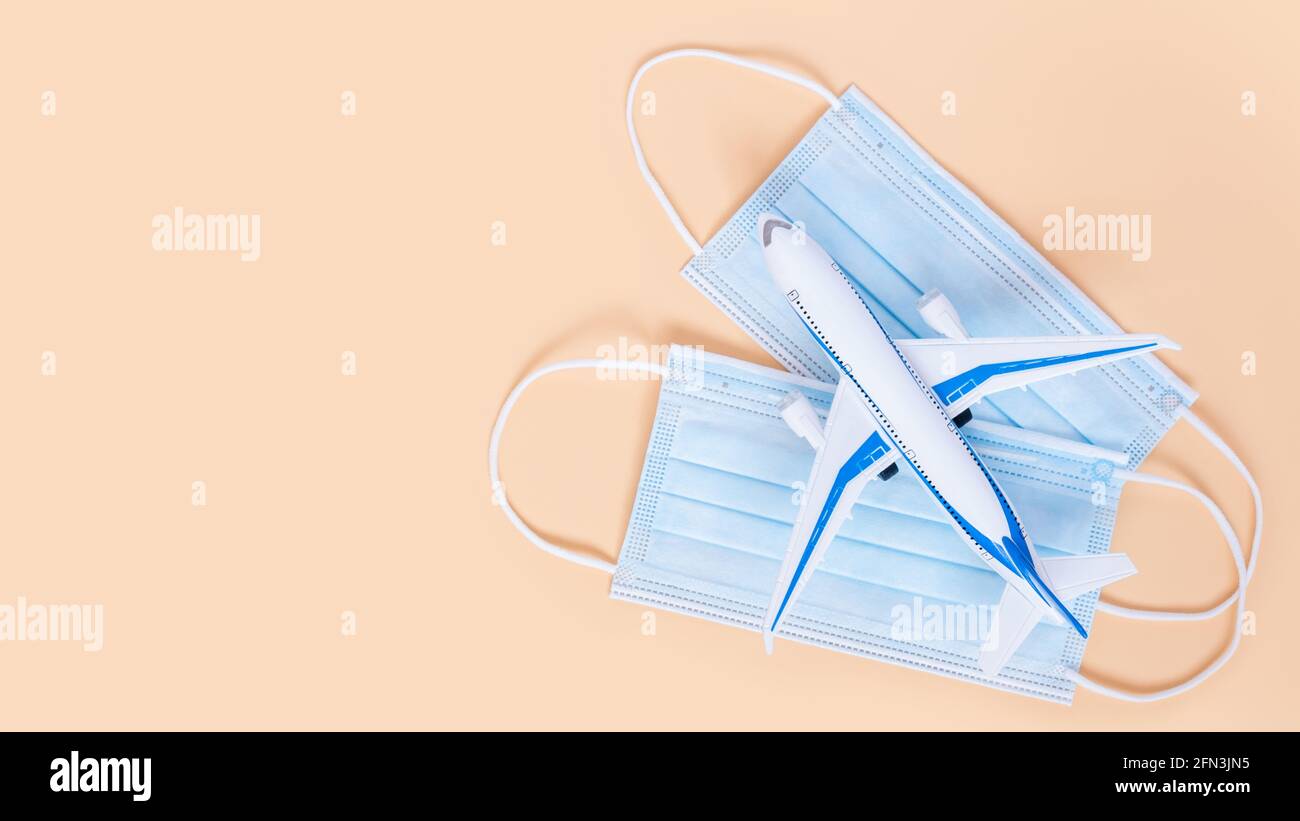 Airplane and medical masks on neutral beige background with copy space ...
