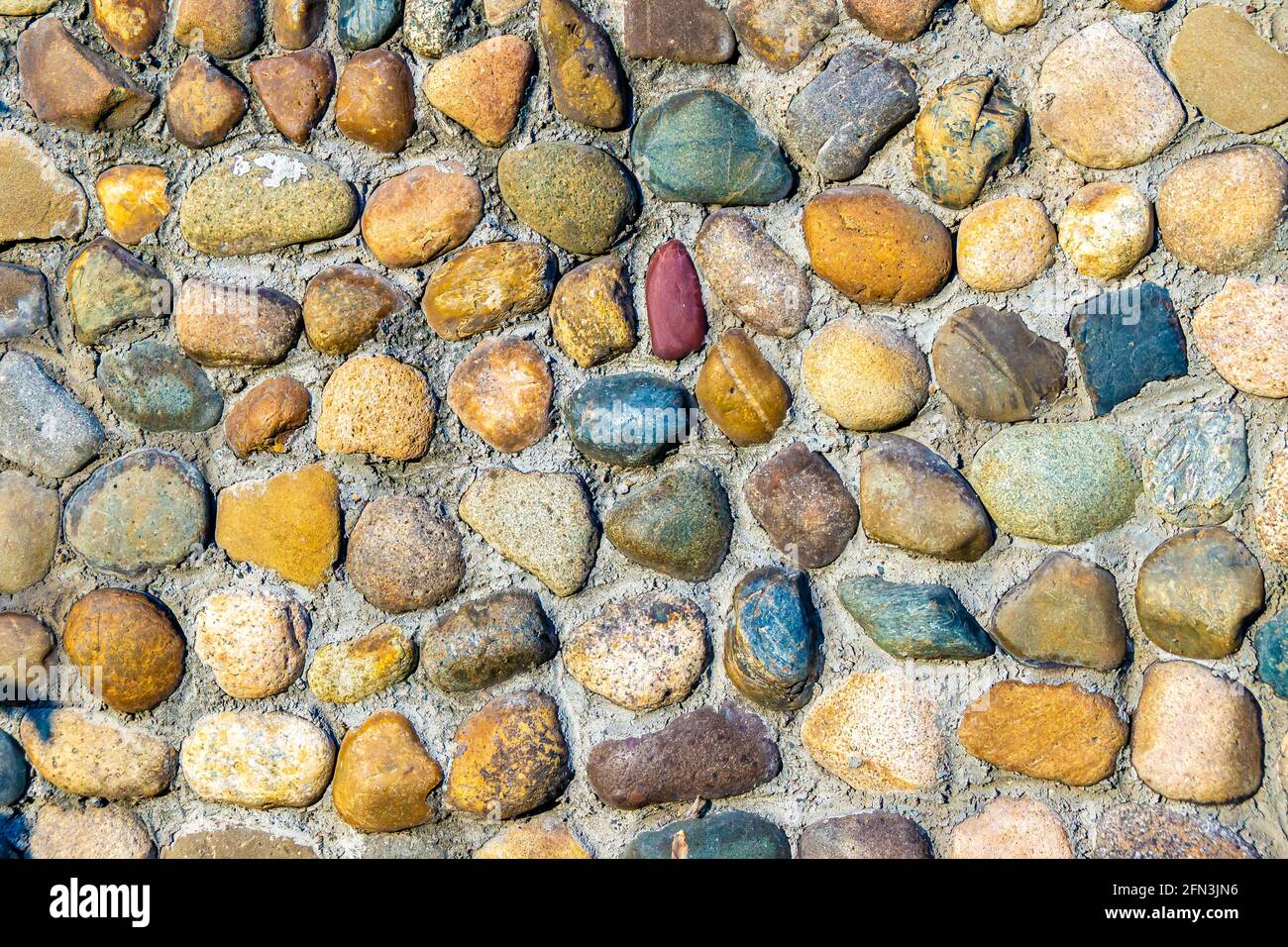 multi-colored and multi-textured pebble stones lie in rows partially ...
