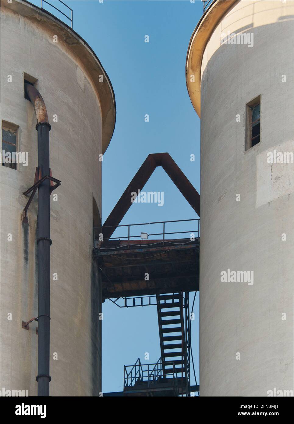 Vertical shot of a pair of round factory towers with stairs leading up ...